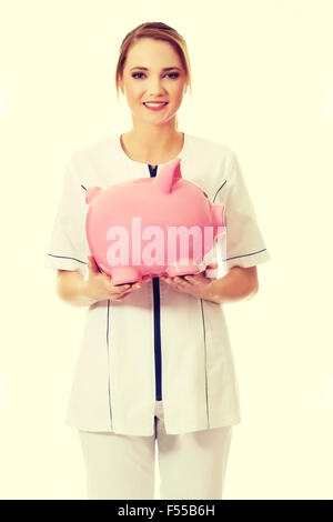 Young doctor woman holding piggy bank smiling with an idea or question ...