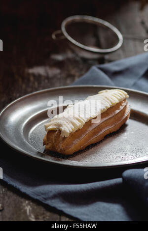 Single Eclair with white butter cream in vintage metal plate with ...