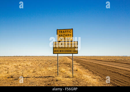 Desert road with rough road sign and distant red cliffs under a clear ...