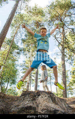 nine year old boy doing star jumps off a bank with his three years old ...