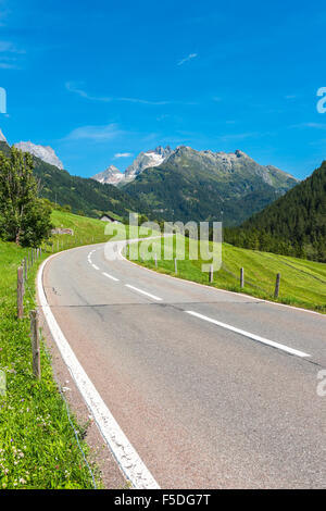 A vertical shot of a narrow asphalt road in a park with a bench near it ...