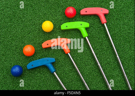 Four mini golf putters and balls of assorted colors laying criss ...