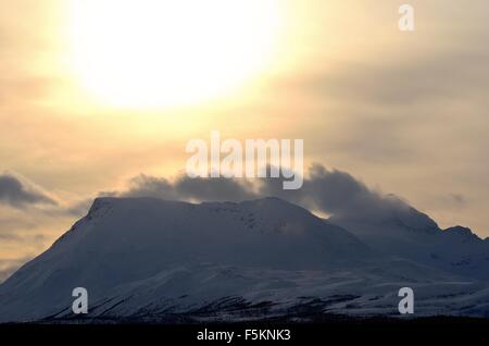 strong sunshine over snowy mountain peak as strong wind blows the snow ...