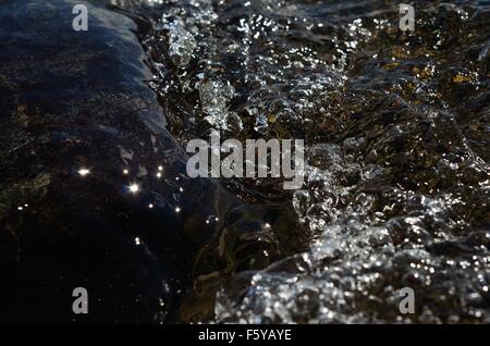 cold river water stream hit a black river rock in summer sunshine Stock ...