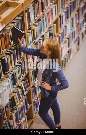 Blond student picking book from bookshelf Stock Photo - Alamy