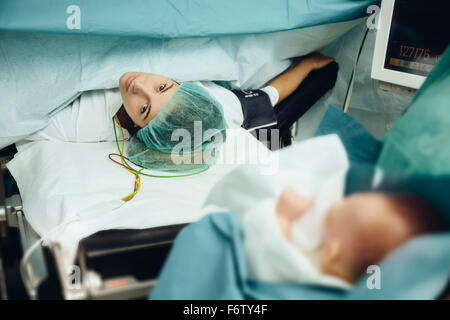 Operating room nurse bringing baby to mother while team finishing c ...