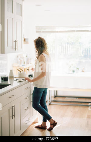 Caucasian woman standing in kitchen preparing food, chopping vegetables ...