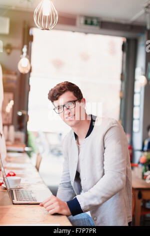 Happy young man using laptop computer while sitting at the kitchen ...
