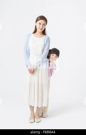 Daughter standing and hiding behind her mother and mother looking at ...