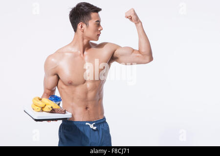 Muscular man showing his biceps and holding a scale with bananas and ...