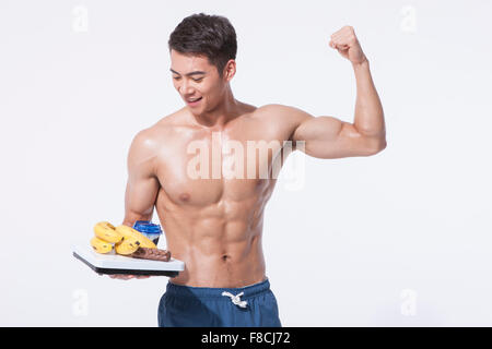 Muscular man holding a scale with bananas and other diet food on it and ...