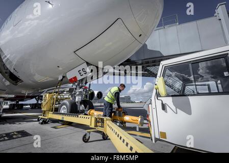 Ground crew attaching a tow bar to an aircraft's nose landing gear with ...