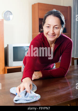 Mature housewife cleaning table with cleanser and rag in living room at ...