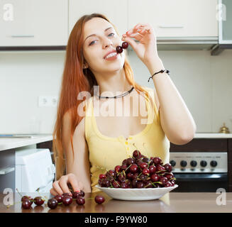 long-haired girl eating cherries at home kitchen Stock Photo - Alamy
