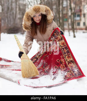 Smiling woman cleans red carpet with snow in winter outdoor Stock Photo ...