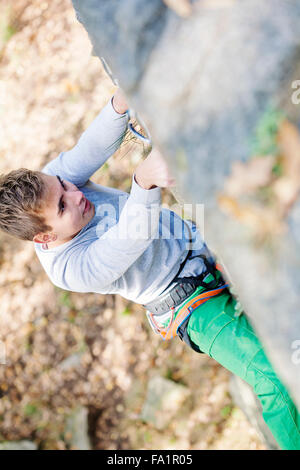 Male climber at top of rock face looking down and pulling on rope Stock ...