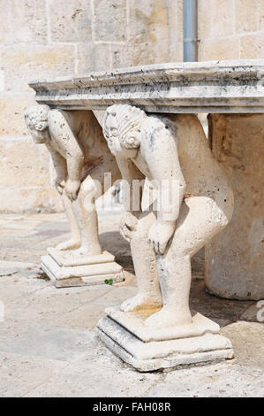 A medieval stone table is supported by two statues of the hunched men ...