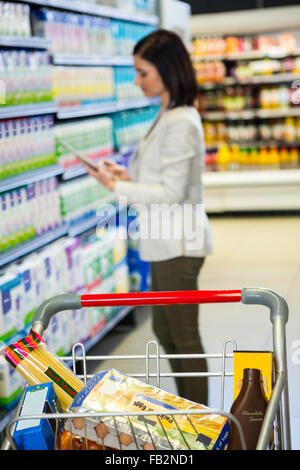 Woman checking a shopping list and trolley full of fresh goods, grocery ...