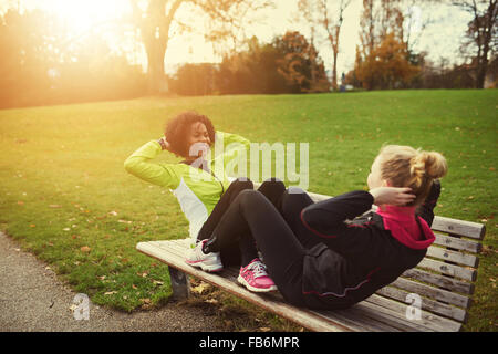 Two smiling women sit on wooden bench sunny park enjoy relax moment ...