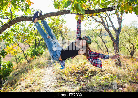 Portrait of young woman swinging from tree branch Stock Photo - Alamy