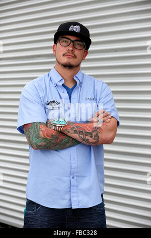 Young hispanic man with beard and tattoos wearing barber apron holding ...
