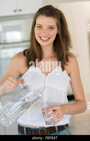 Young woman pouring water into glass on blue background Stock Photo - Alamy