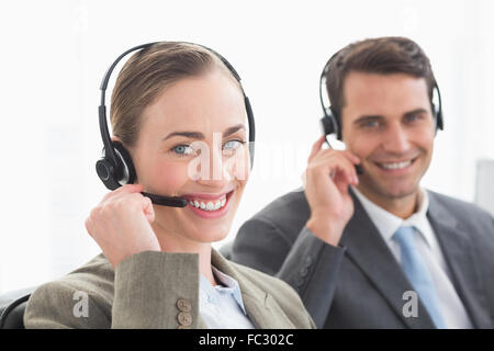 Smiling business executives with headsets using computers at desk in ...