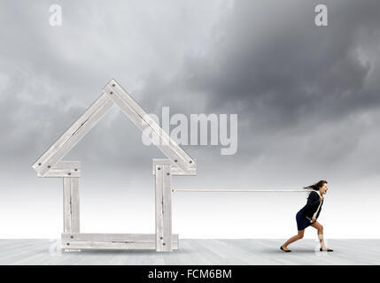 Young determined businesswoman pulling wooden house model Stock Photo ...