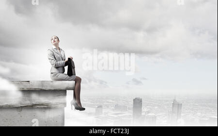 Fearless businesswoman with suitcase sitting on building top Stock ...