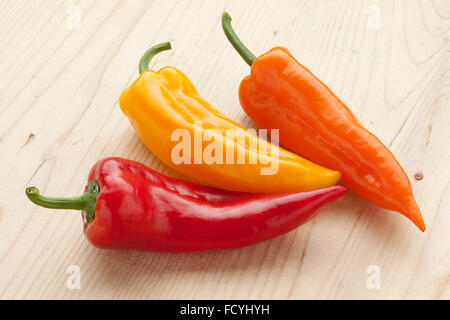 Red, Orange and yellow sweet pointed peppers on a wooden cutting board ...