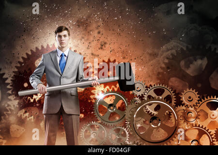 Young businessman with hammer against gears background Stock Photo - Alamy