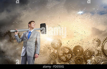 Young businessman with hammer against gears background Stock Photo - Alamy