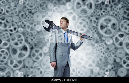 Young determined businessman with wrench on shoulder and cogwheels at ...