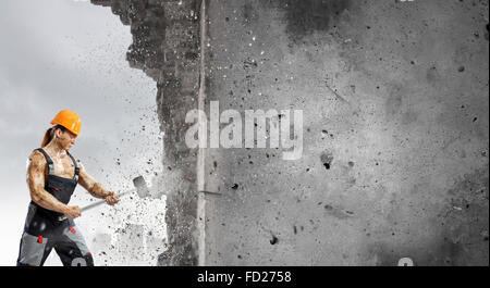 Strong man in uniform breaking brick wall with hammer Stock Photo - Alamy