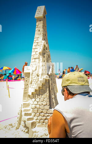 A man works on an elaborate sandcastle construction reminiscent of ...