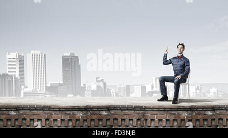 Young funny guy sitting in chair and pointing upwards Stock Photo - Alamy