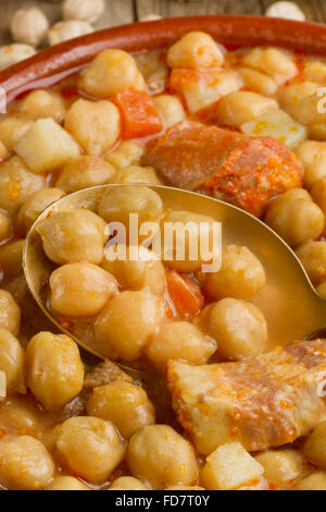 Spanish Cocido in an earthenware pot, golden fork and spoon on a white ...