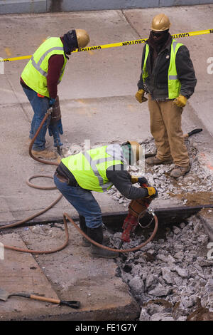 2 construction workers with jackhammers break up concrete on a city ...