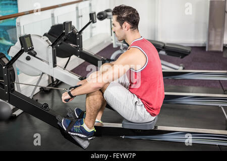 Muscular man on rowing machine using smart watch Stock Photo - Alamy