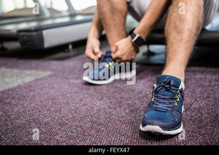 Lower section of man sitting on treadmill and tying the shoelace Stock ...