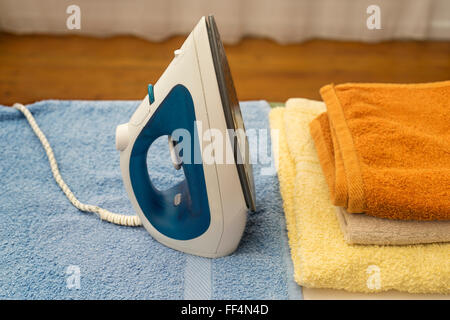 Stack of towels and electric iron on light pink background Stock Photo ...