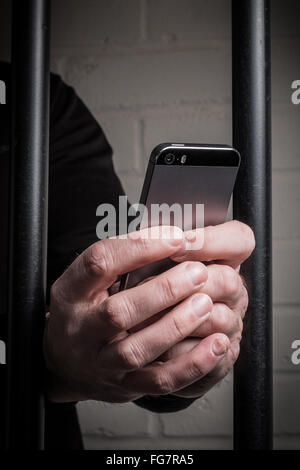 A prisoner in prison using a mobile phone behind bars in a cell Stock ...