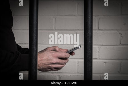 A prisoner in prison using a mobile phone behind bars in a cell Stock ...