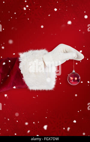 Santas hand is holding a Christmas bulb against red snowflake ...