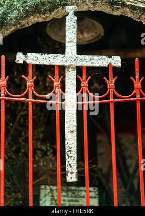 A stone wall with a black gate and a stone cross on the ground. The ...