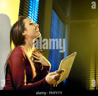 Laughing woman using cellphone and tablet computer while lying on sofa ...