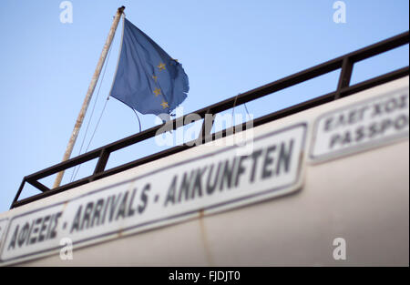 A large European Union flag waves above a paved plaza where a woman ...