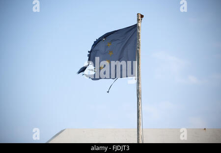 A large European Union flag waves above a paved plaza where a woman ...