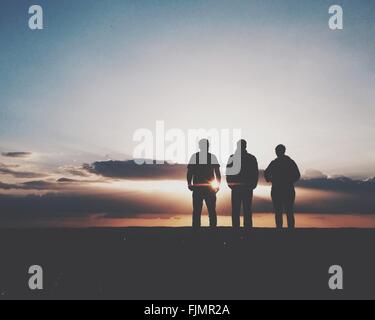 Three people standing in the sea at sunset off a beach in western Sabah ...