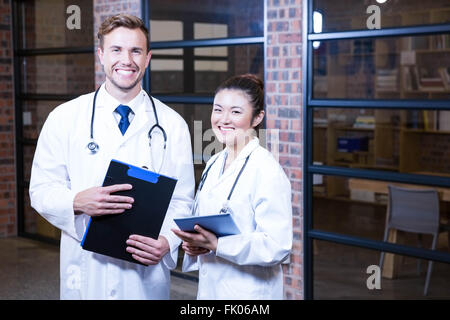 Portrait of doctors standing near library with clipboard and digital ...